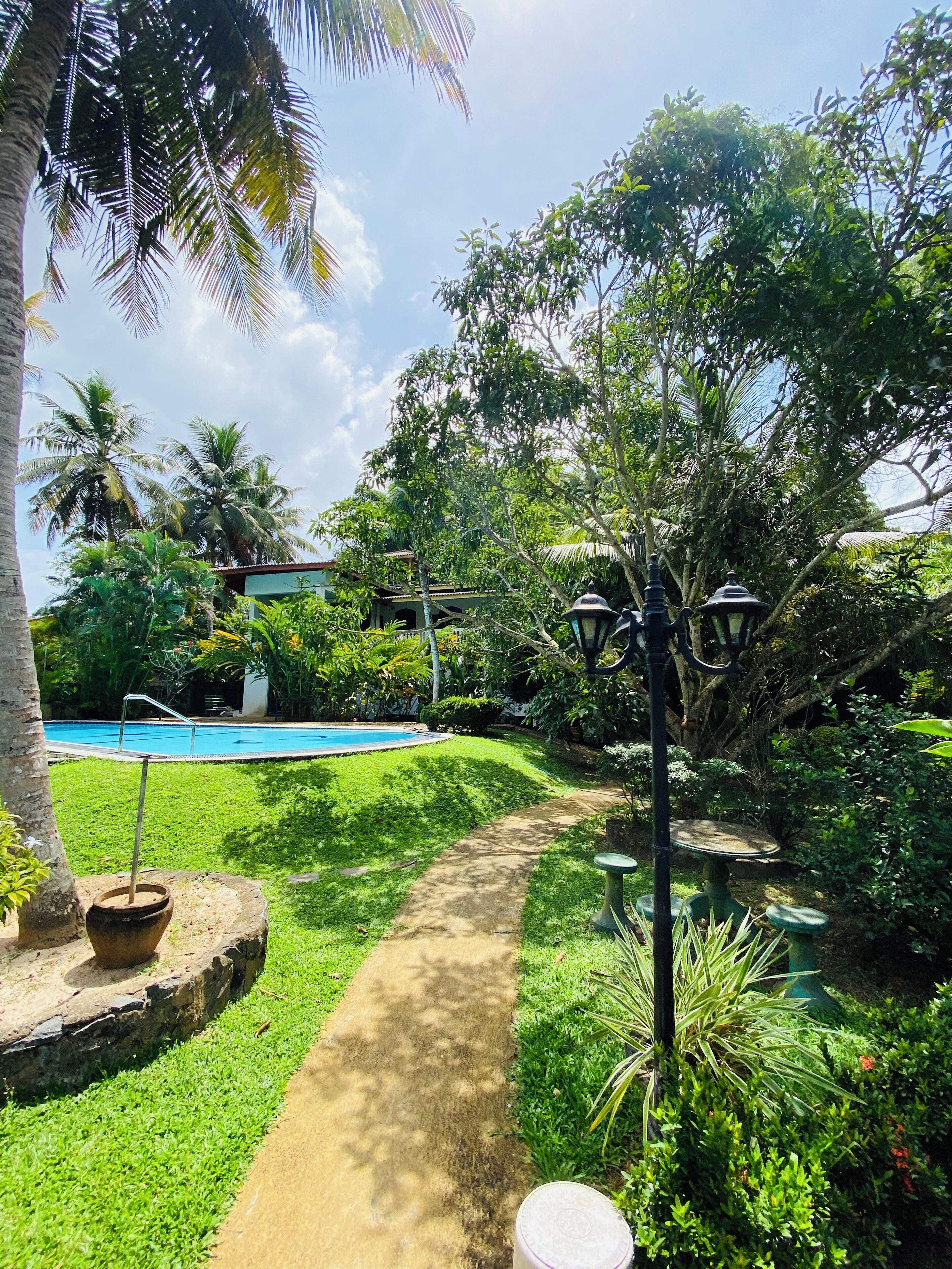 Um jardim exuberante com piscina, um caminho pavimentado e área de estar ao ar livre.