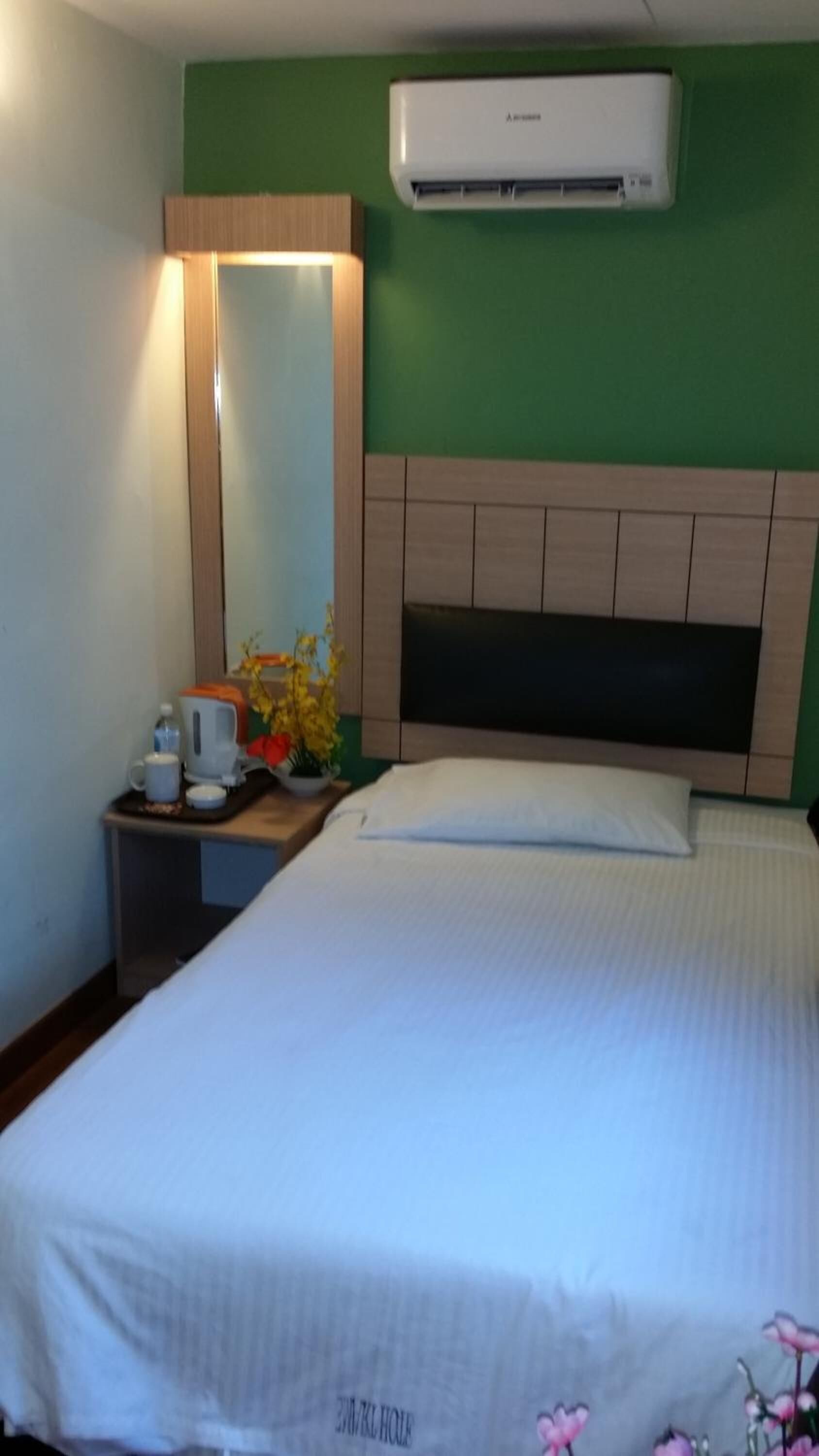 Quarto de hotel com cama, mesa de cabeceira, espelho, ar condicionado e parede verde.