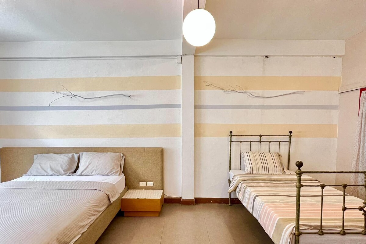 Quarto com duas camas, luminária pendente e design de parede listrado.