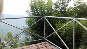 Corrimão de metal com piso ladrilhado, cercado por vegetação e montanhas ao fundo.