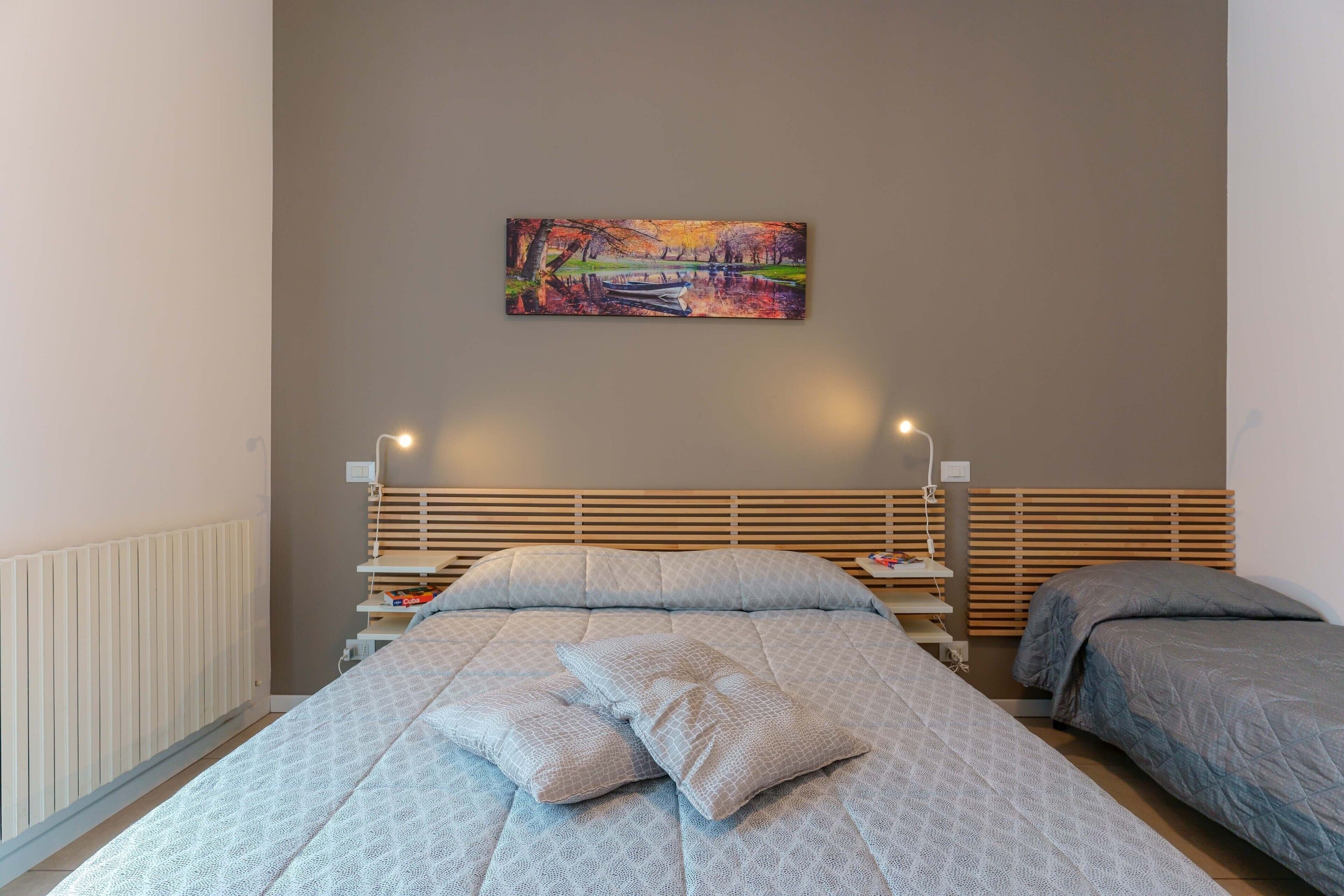 Quarto com uma cama, duas mesas de cabeceira, um criado-mudo, um quadro na parede e um radiador.