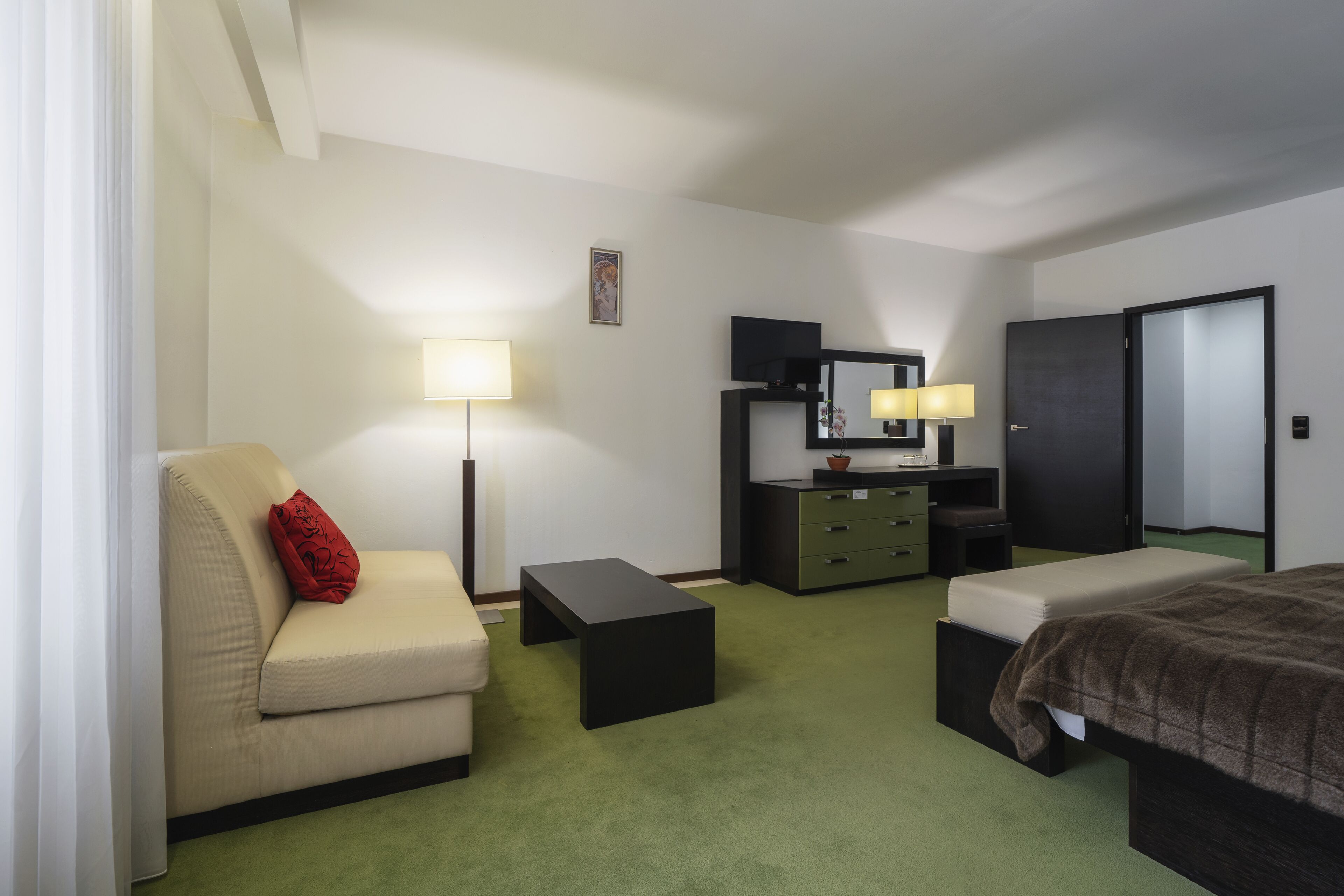 Quarto de hotel com sofá, cama, escrivaninha com computador, televisão e guarda-roupa.