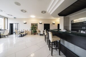 Um lobby moderno de hotel com área de bar, sofás e uma grande planta em vaso.