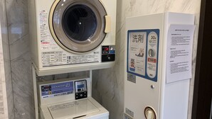 Máquina de lavanderia automática com visor digital, entrada para moedas e painel de controle. Instruções visíveis na lateral da máquina.