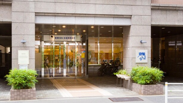 Entrada de hotel com porta de vidro, placa de identificação e plantas em vasos.