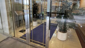Um saguão de hotel moderno com portas de vidro, plantas em vasos e carpete azul.