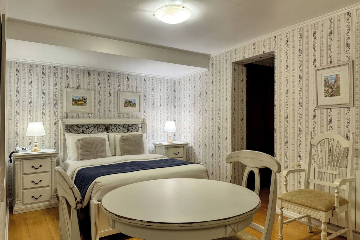 Quarto com cama, mesas de cabeceira, uma mesa redonda e duas cadeiras.