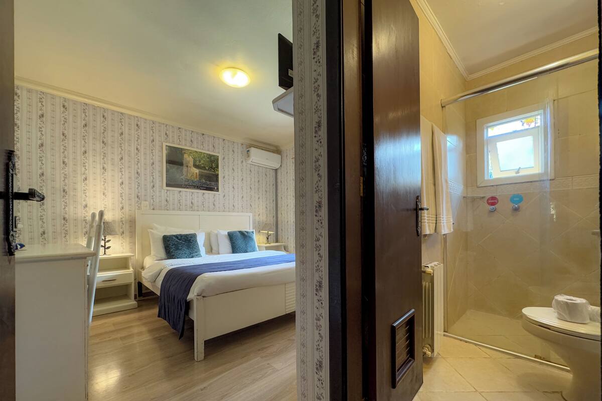 Quarto de hotel com cama, mesa de cabeceira, luminária e vista para o banheiro.
