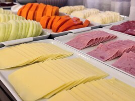 Buffet com queijo fatiado, presunto e cenouras dispostos de forma organizada.