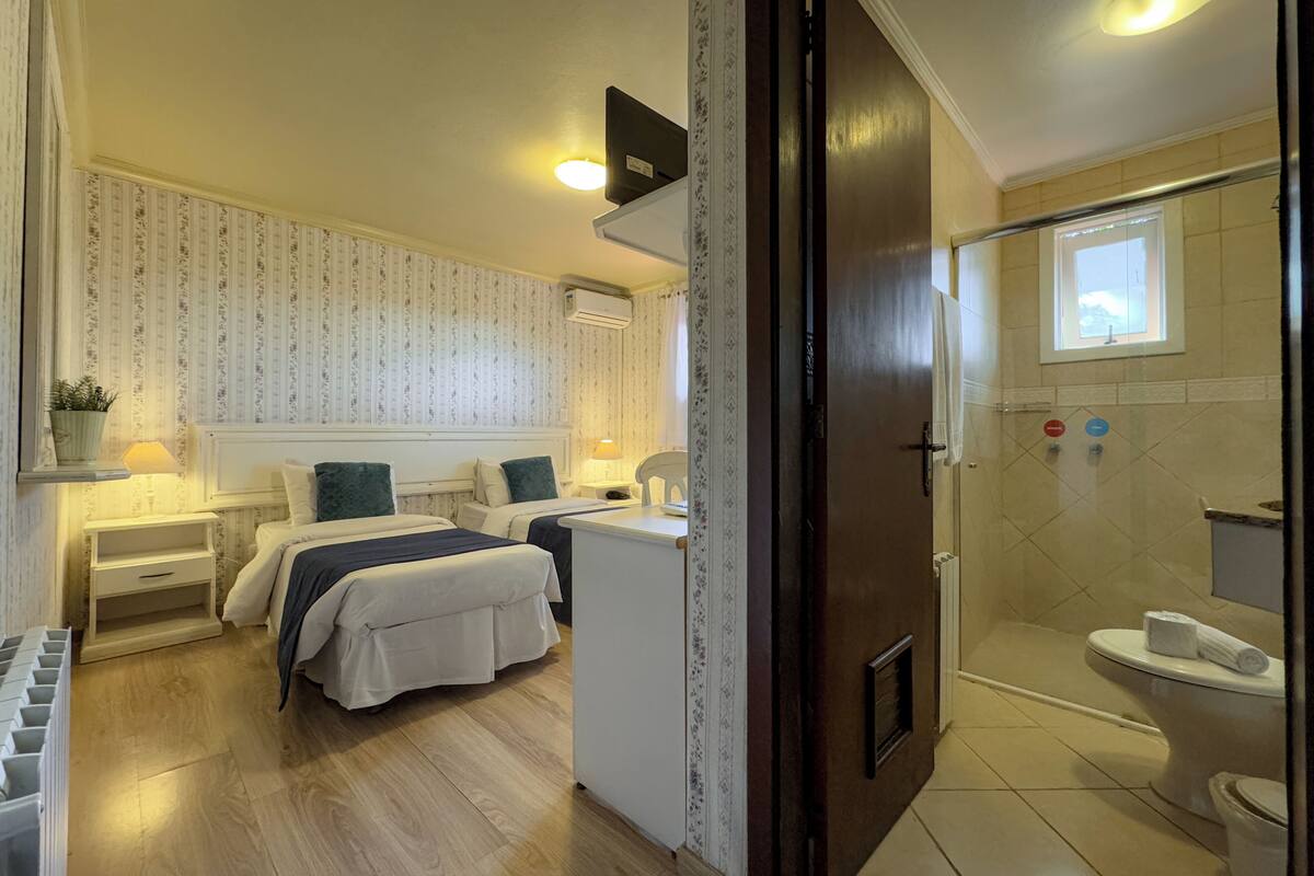 Quarto de hotel com duas camas, chuveiro e sanitário.