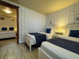 Quarto de hotel com duas camas, piso de madeira e papel de parede listrado.