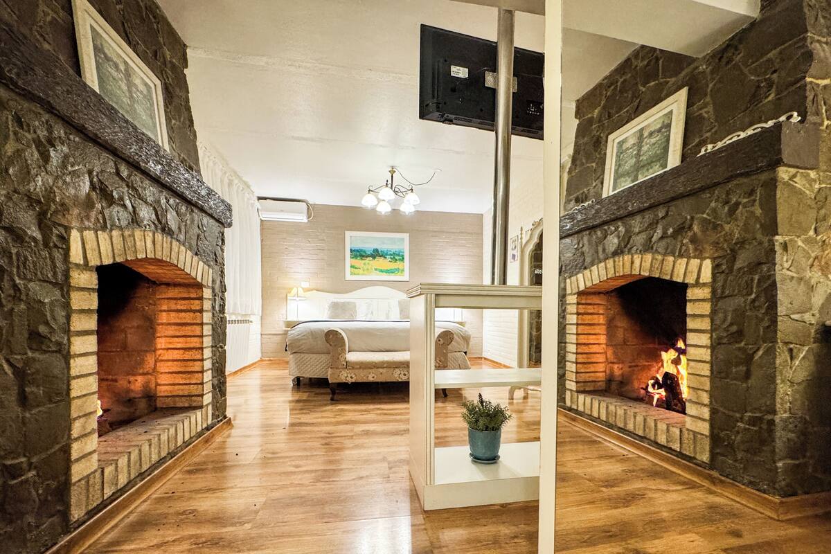 Um quarto com duas lareiras de pedra, assoalho de madeira, um sofá branco e um quadro na parede.