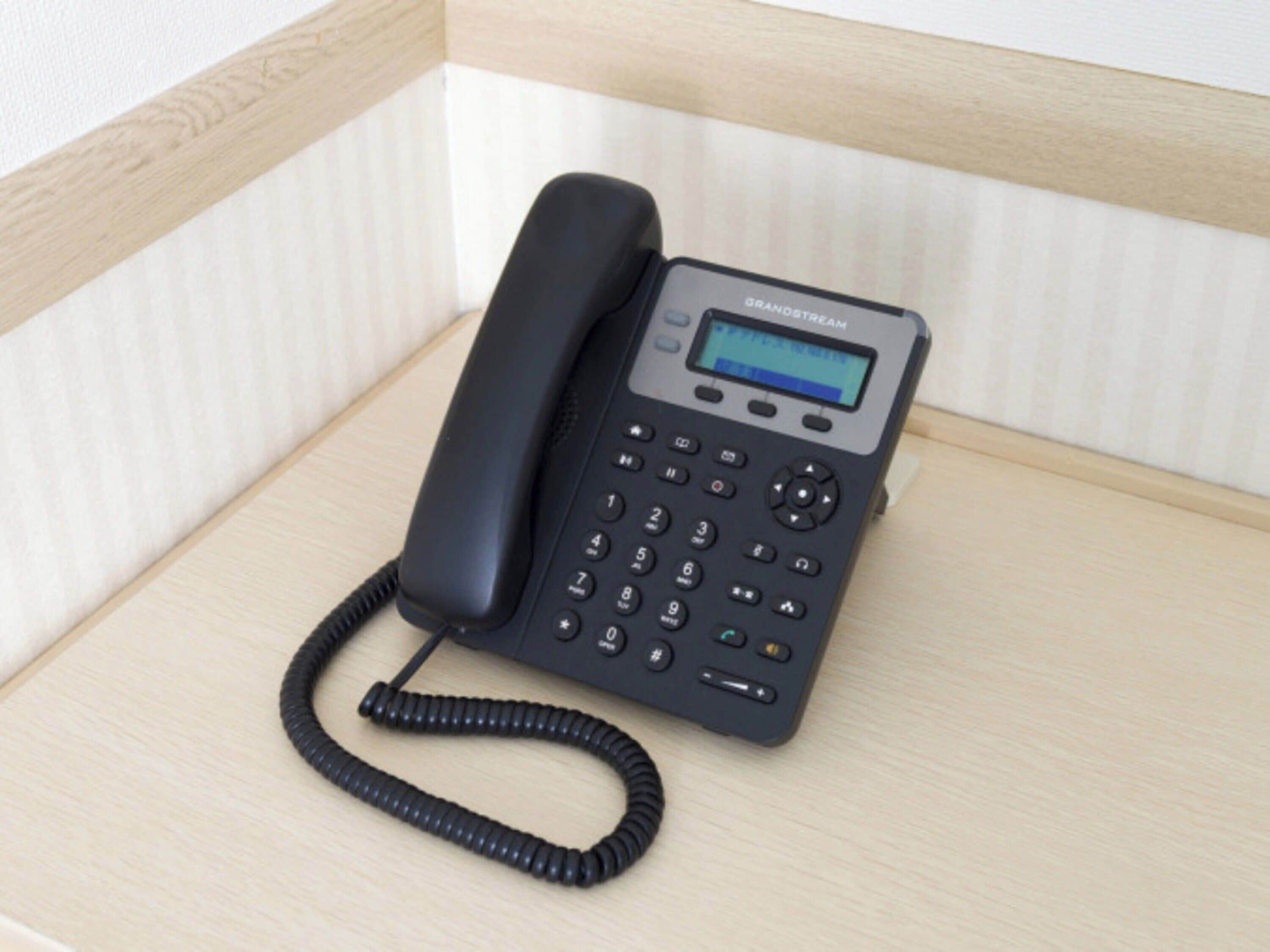 Um telefone de mesa preto com teclado e uma tela pequena, sobre uma escrivaninha de madeira.