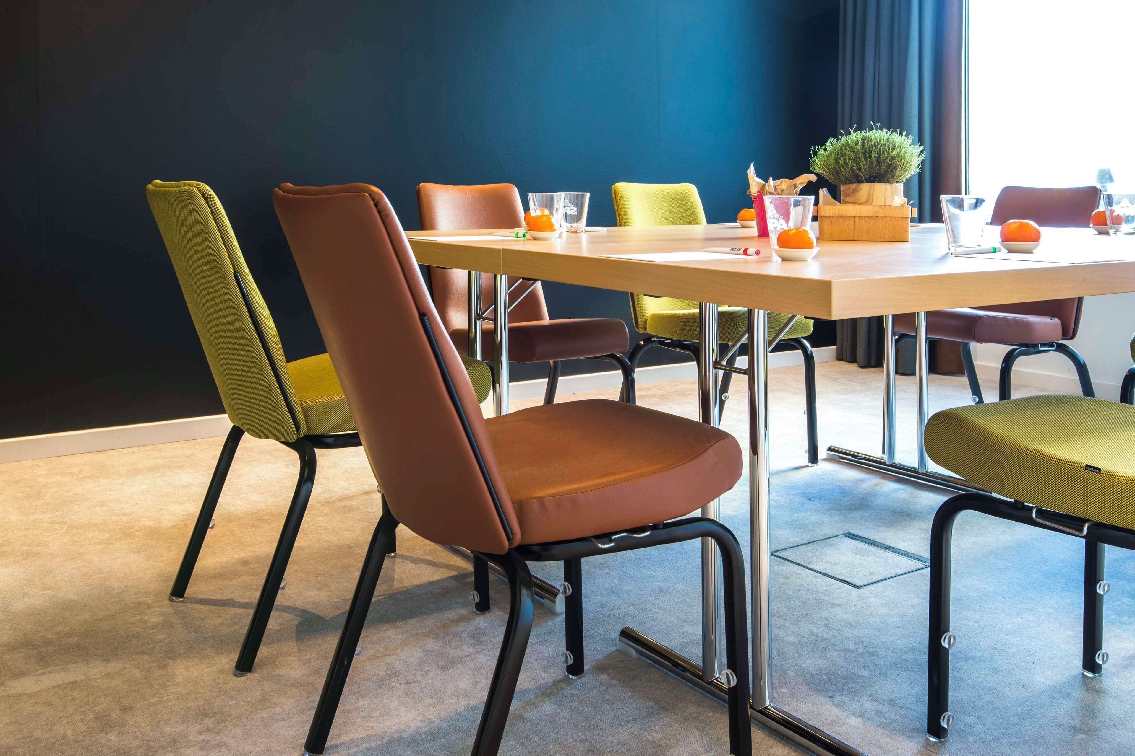 Uma sala de conferências com uma mesa comprida, várias cadeiras e um vaso de planta na mesa.