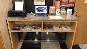 Uma mesa de recepção com uma impressora, um laptop e diversos folhetos informativos.