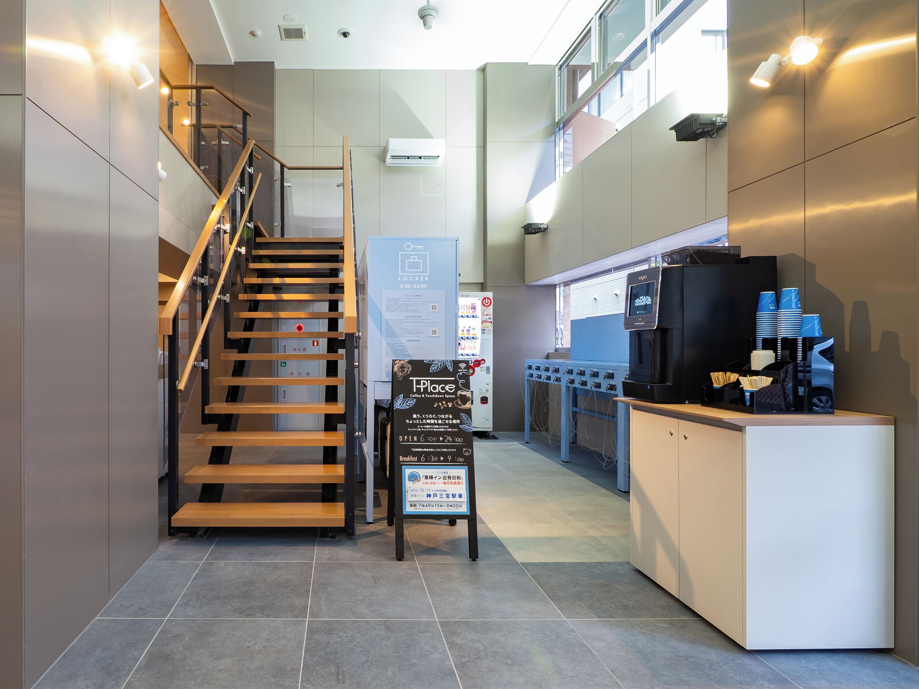 Um saguão de hotel moderno com uma escada, um balcão de recepção e uma máquina de café.