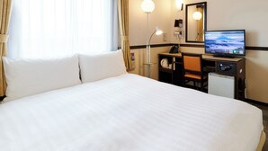 Quarto de hotel com uma cama grande, uma escrivaninha com computador, televisão e um pequeno frigorífico.