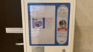 Casa de banho pública com esquema de cores azul e branco, compartimento para moedas de 30 ienes e um aviso a pedir atenção à saúde durante a utilização.