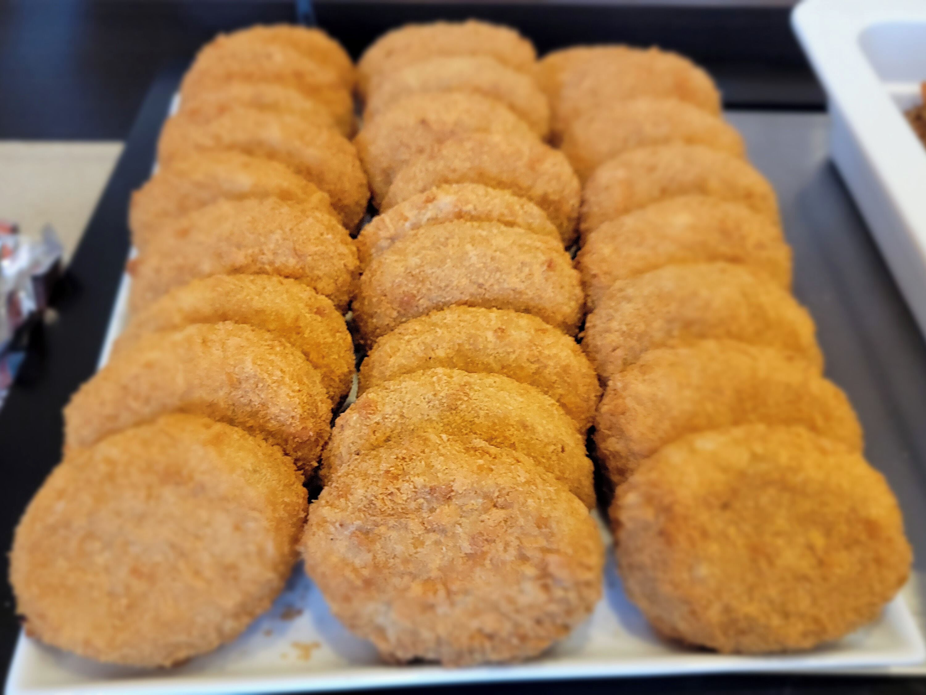 Uma bandeja com várias porções de comida frita, redonda e dourada, dispostas em fileiras.