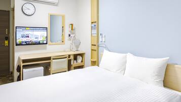 Quarto de hotel com cama, escrivaninha com monitor de computador, espelho e ar condicionado.