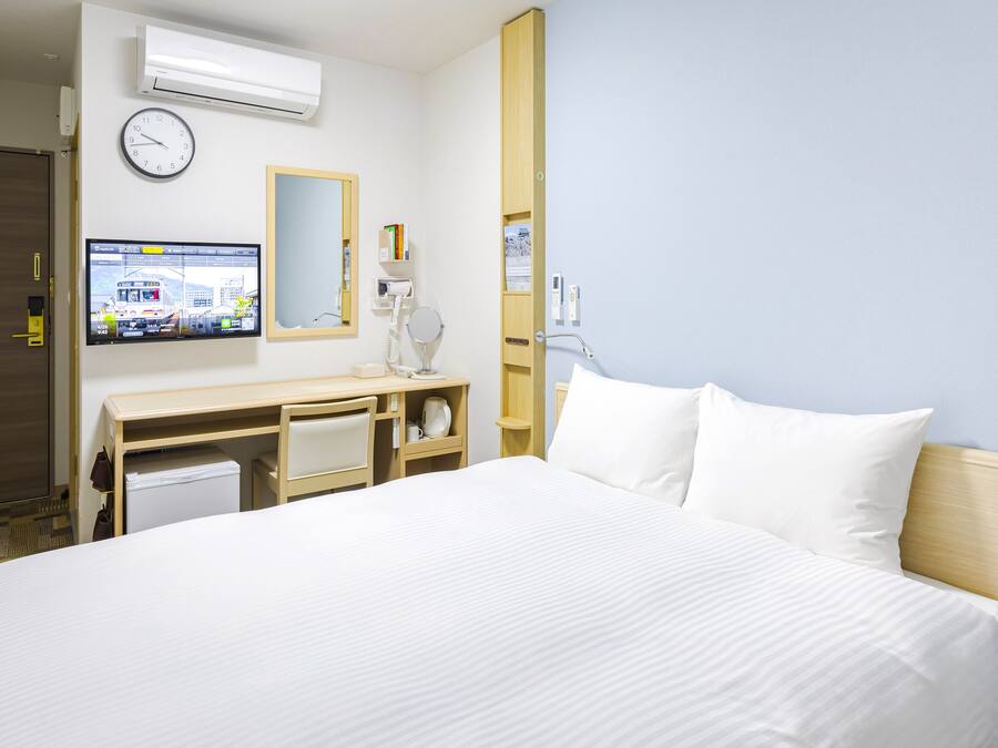 Quarto de hotel com cama, escrivaninha com monitor de computador, espelho e ar condicionado.