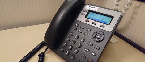 Um telefone de mesa preto com visor, o número 507, sobre uma escrivaninha bege.