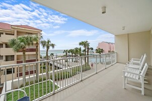 Uma varanda com vista para a praia, piscina e palmeiras.