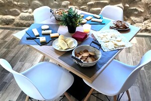 Uma mesa posta para refeição, com diversos queijos, pão e um vaso de planta.