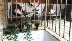 Varanda de madeira com guarda-corrimão de metal, plantas em vasos e mobiliário de vime.