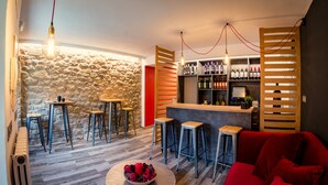 Uma área de bar com banquetas, balcão com garrafas e parede de pedra.