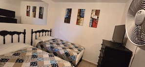 Quarto com duas camas, penteadeira, televisão e obras de arte na parede.