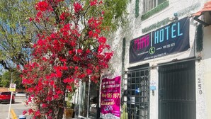 Um hotel com uma placa, uma árvore com flores vermelhas e o símbolo de acessibilidade para cadeiras de rodas.