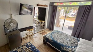 Um quarto com cama, escrivaninha, cadeira, televisão e janela com cortinas.
