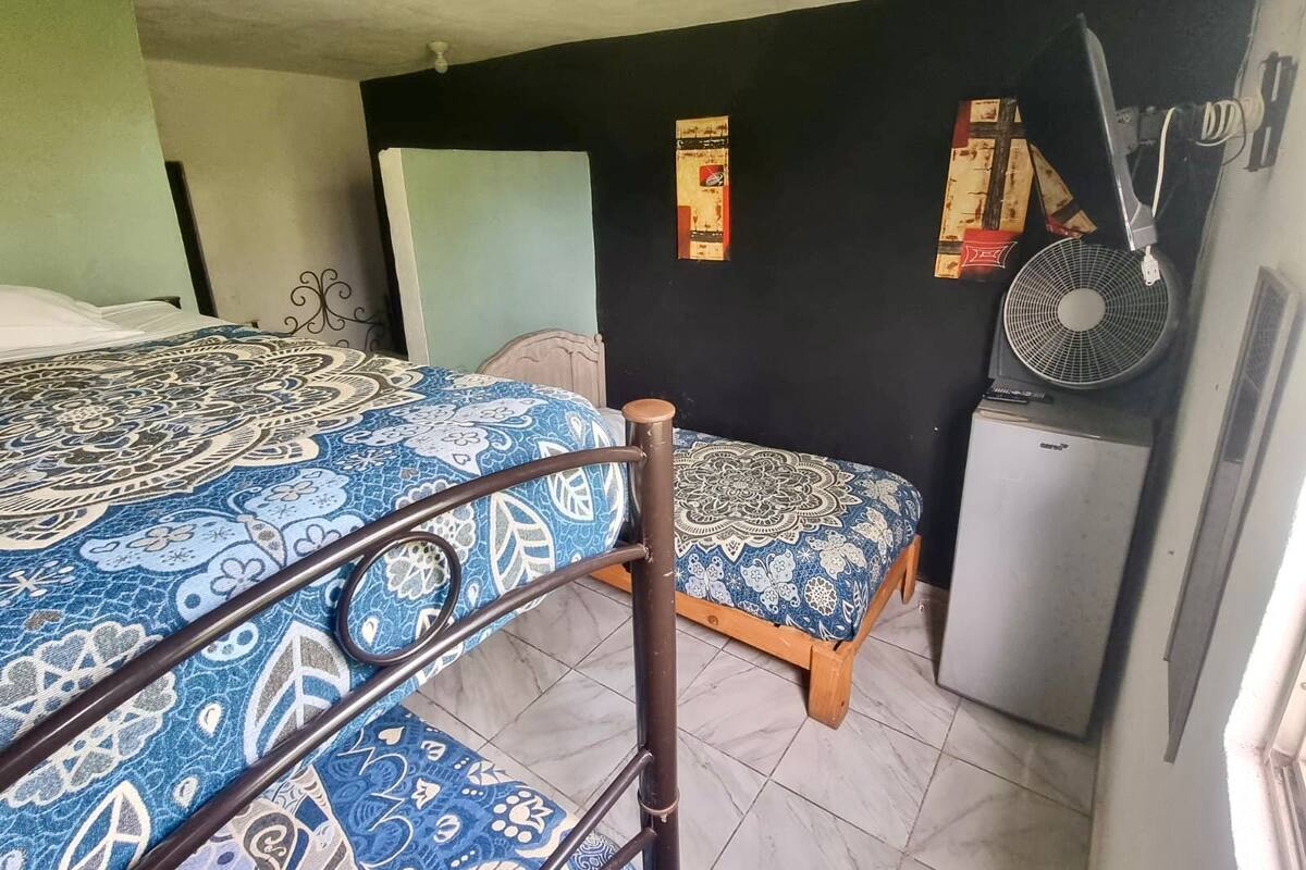 Quarto pequeno e compacto com cama, escrivaninha e geladeira.