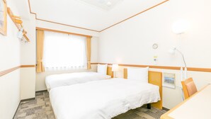 Quarto de hotel com duas camas, uma escrivaninha, uma cadeira, um abajur, um relógio e uma janela com cortinas.
