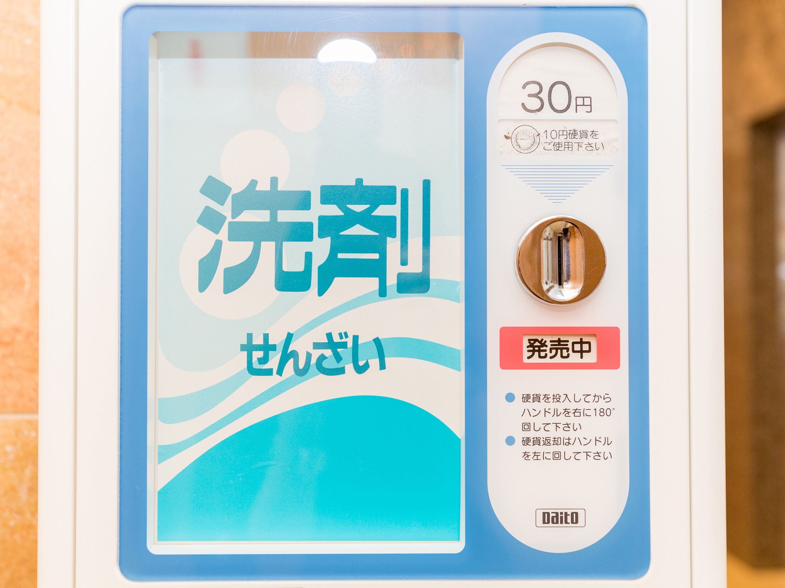 Um banheiro público com design azul e branco, um dispensador de moedas e instruções em japonês.