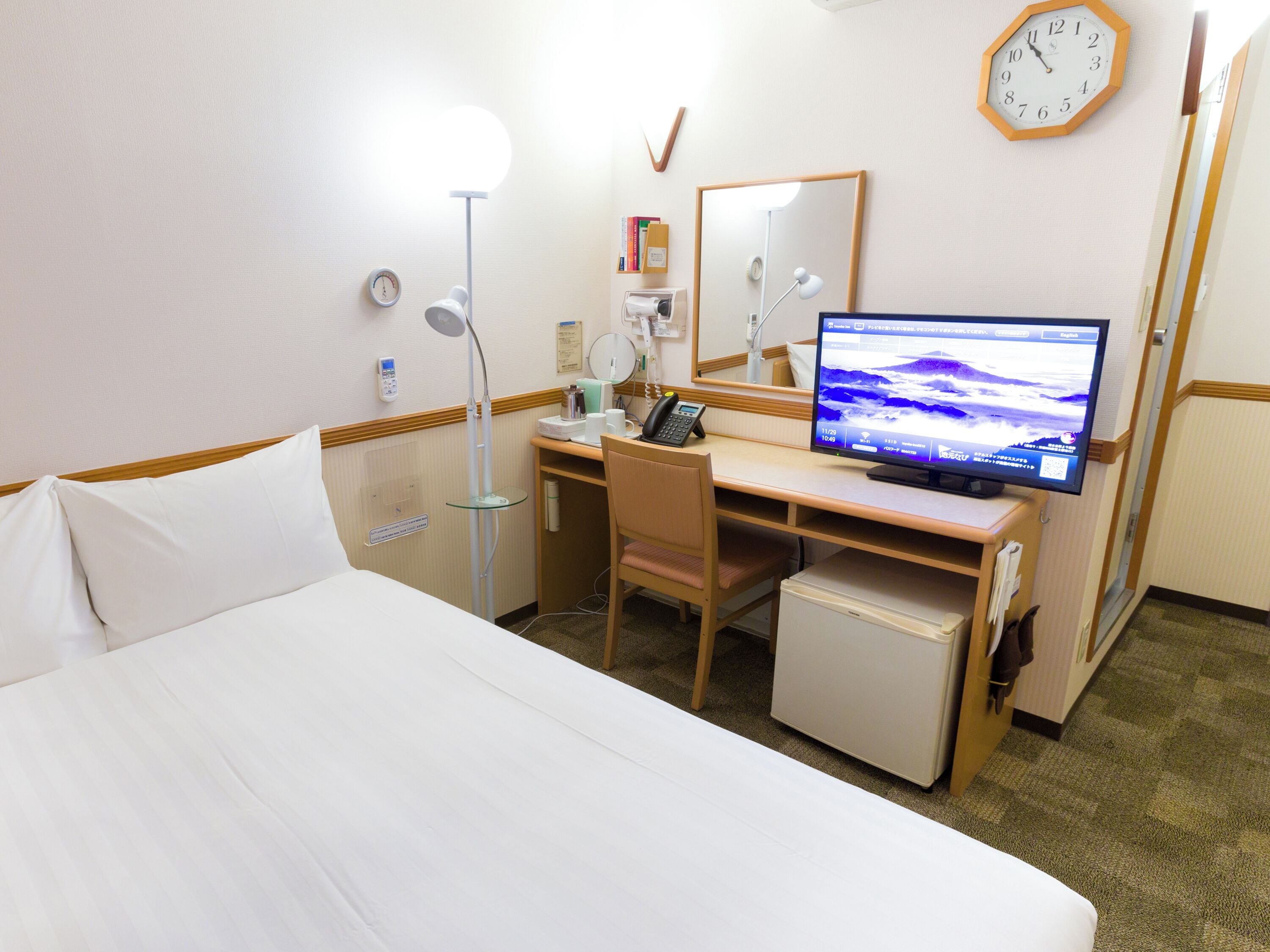 Quarto de hotel com cama, escrivaninha, cadeira e um pequeno frigorífico.