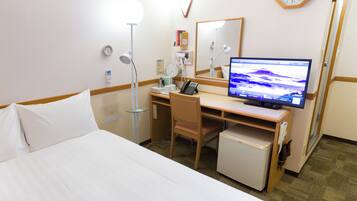 Quarto de hotel com cama, escrivaninha, cadeira e um pequeno frigorífico.