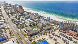 Vista aérea de uma cidade costeira com um hotel na praia, uma avenida principal e um estacionamento.