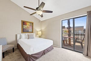 Quarto de hotel com cama, uma cadeira, um quadro, ventoinha no teto, varanda com mesa e cadeiras, e vista para edifícios.