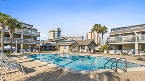 Piscina com espreguiçadeiras e palmeiras, cercada por edifícios altos com varandas.