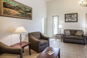 Sala de estar com sofá, poltrona e mesa de centro. Há duas luminárias, um quadro na parede e uma janela com cortinas.