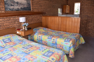 Quarto com duas camas, uma cabeceira de madeira, uma mesinha com abajur e um quadro na parede.