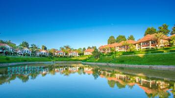 Vista serena de um lago, com várias casas, céu claro e águas calmas que refletem a paisagem.