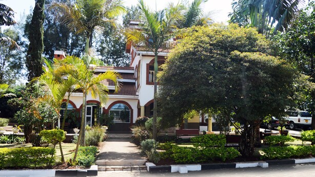 Um edifício de dois andares com telhado de azulejos, cercado por vegetação exuberante e palmeiras.