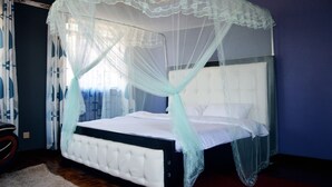 Quarto com cama de dossel, cabeceira branca e piso de madeira.