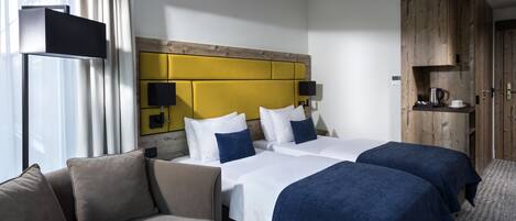 Quarto de hotel com duas camas, um sofá, um guarda-roupa de madeira e uma mesa de centro.