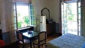 Quarto com cama, escrivaninha com cadeira, televisão e cómoda.