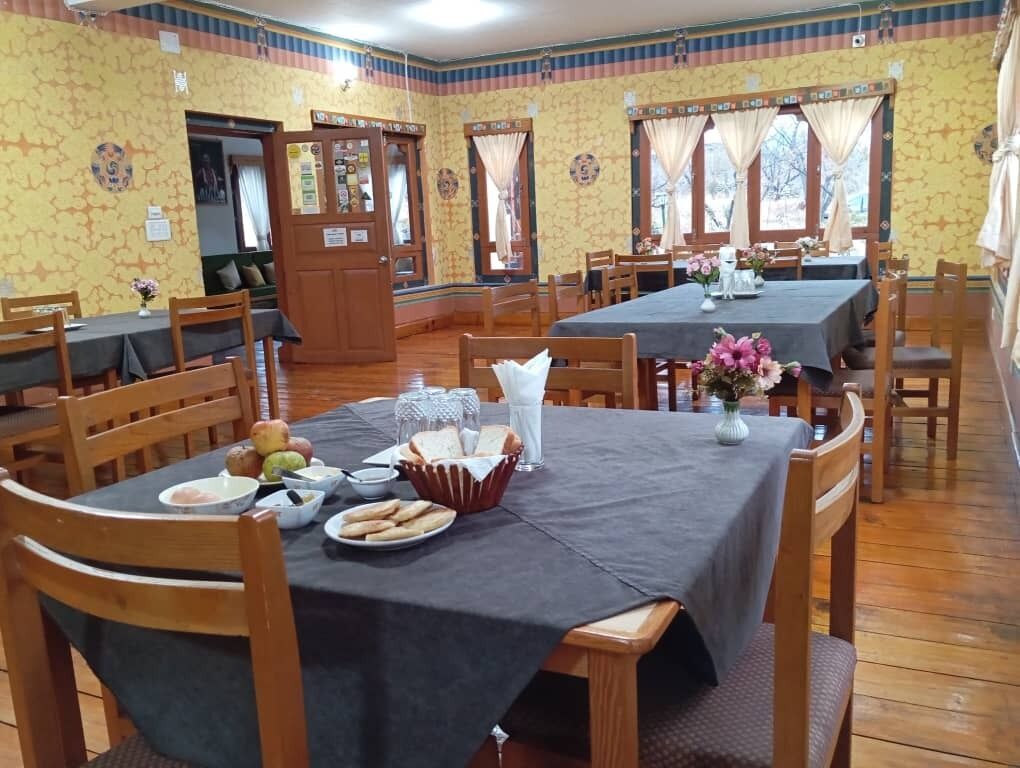 Uma sala de jantar com mesas postas, cadeiras de madeira e um papel de parede estampado.
