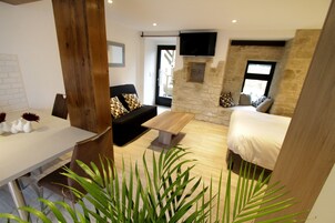 Uma sala de estar moderna com lareira de pedra, um sofá, uma cama e um espaço de jantar com mesa e cadeiras.